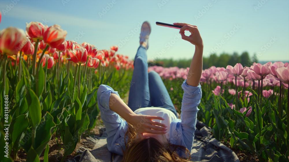 Relaxed young woman swinging legs in blue sky background in tulip field ...