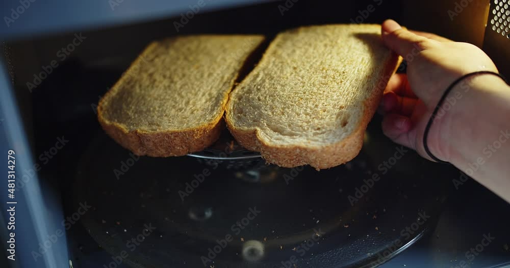 close up woman hand putting fresh slices bread into the microwave grill ...