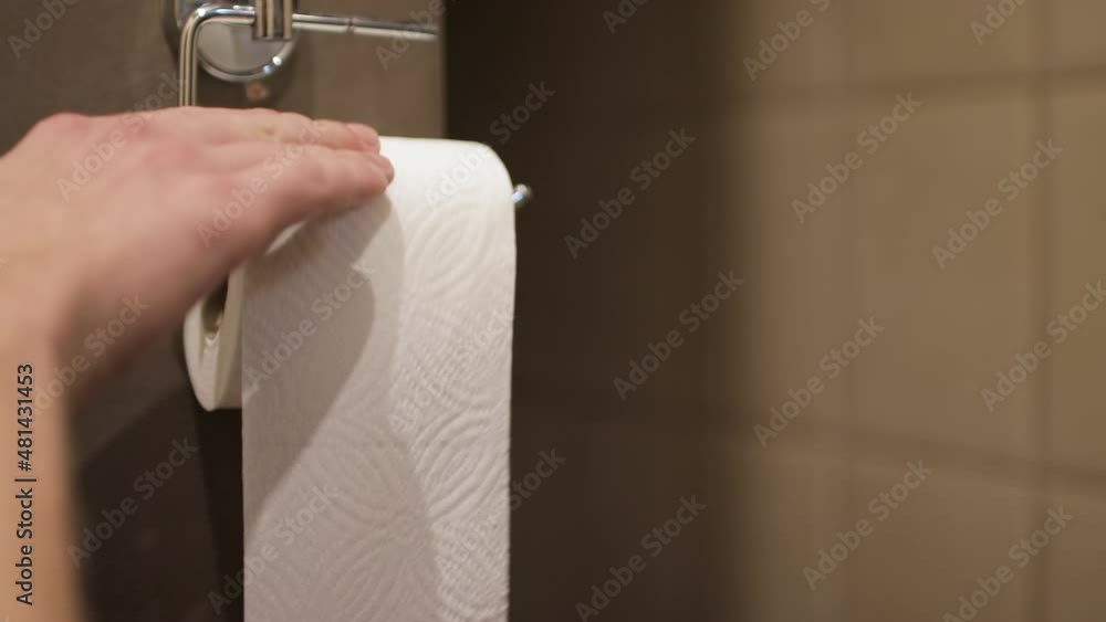 Hands taking toilet paper from a wall mounted toilet paper roll ...