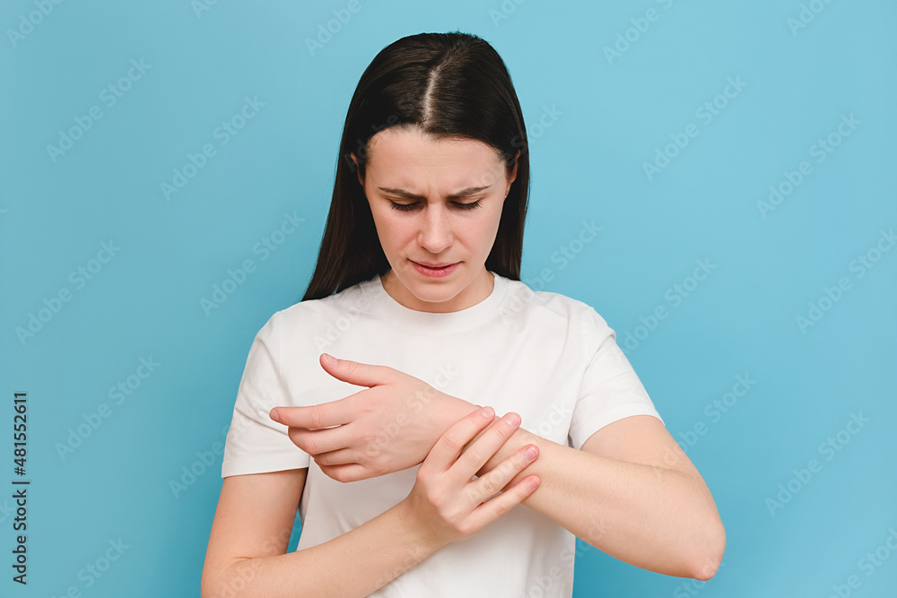 Portrait of tired young female arms holding her painful wrist caused by ...