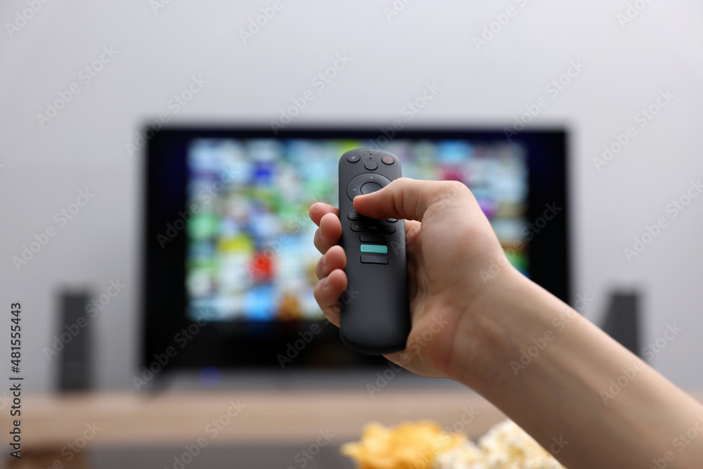 Woman switching channels on TV set with remote control at home, closeup ...