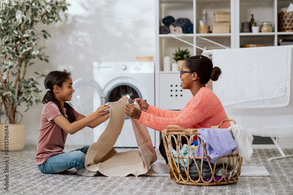 Mother and daughter are sitting on floor in home laundry room, the girl ...
