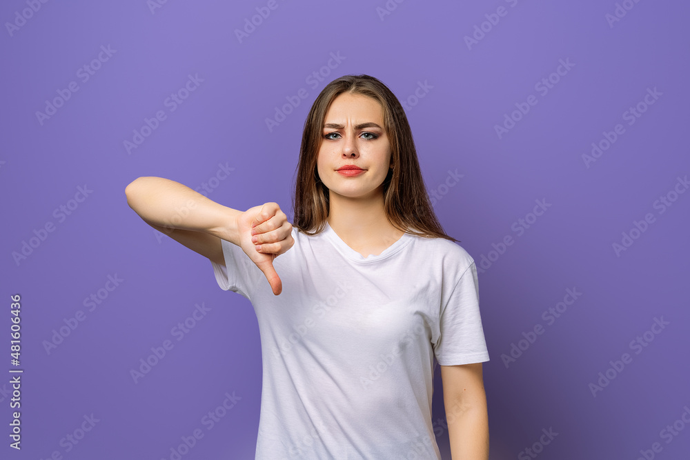 Dissatisfied young brunette woman showing her thumb down in disapproval ...