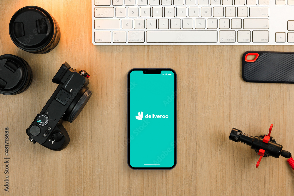 Deliveroo app on smartphone iPhone 13 screen on wooden table. Content ...