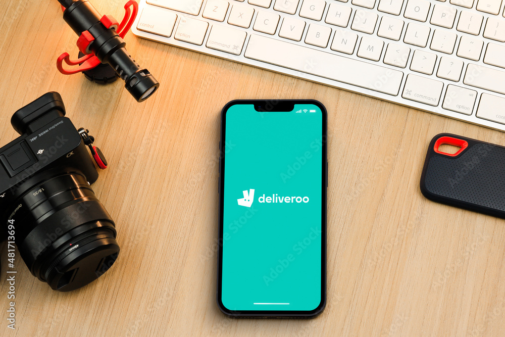 Deliveroo app on smartphone iPhone 13 screen on wooden table. Content ...