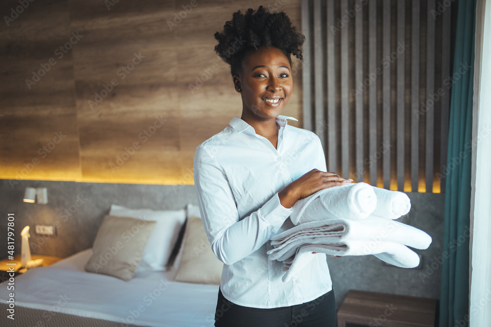 African american house keeper at a guest bedroom holding towels while ...