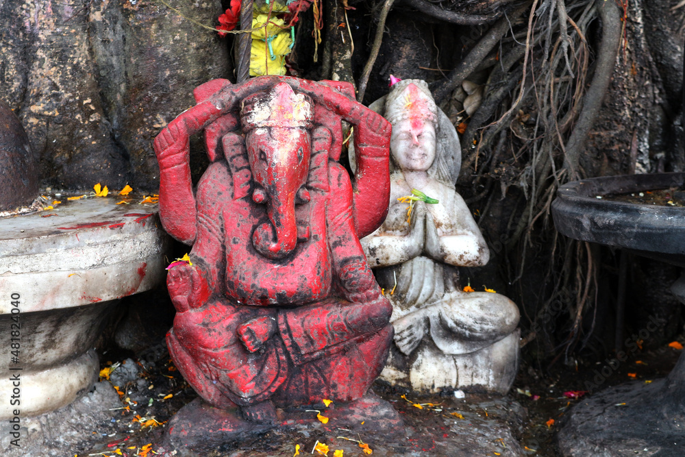 Red sculpture of the Indian god Ganesha under a tree. A makeshift Hindu ...