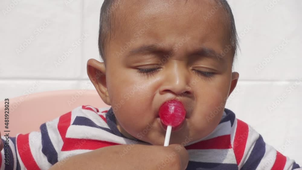 The cute baby boy is trying to eat a red lollipop. Infant baby eating ...