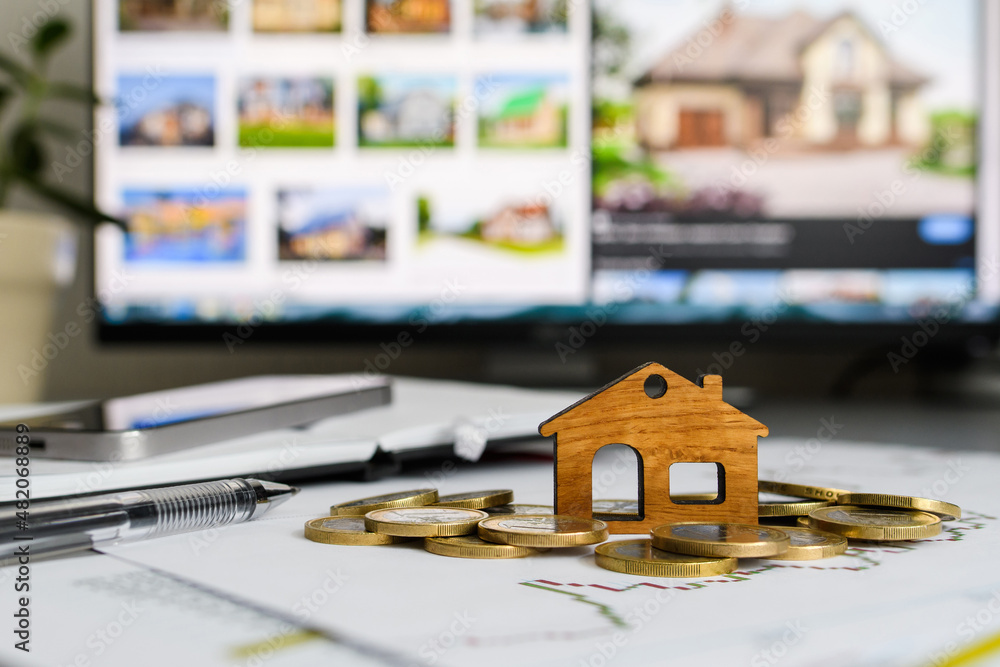 A small wooden house with coins on a computer background with a picture ...