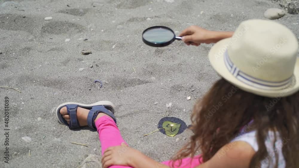 Schoolgirl lights a fire through a magnifying glass in the park. Girl ...