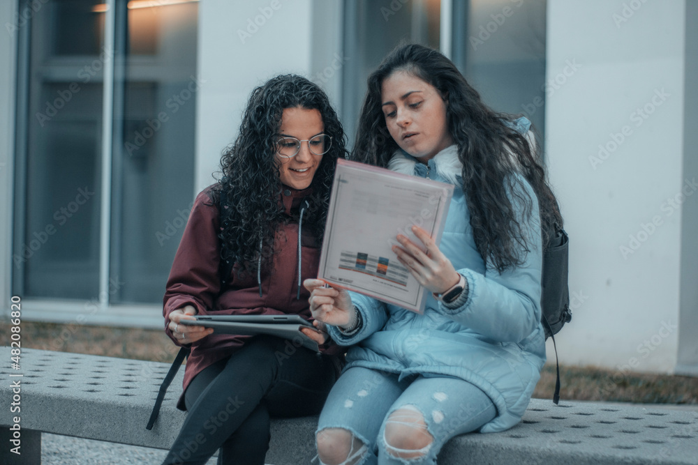 Muchachas estudiantes sentadas en el campus universitario revisando sus ...
