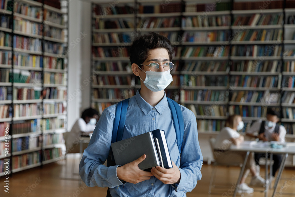 Thoughtful young fresh student wearing facial medical mask protecting ...