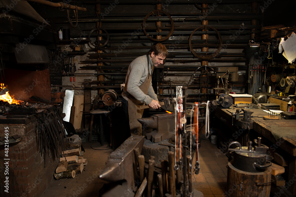Poster portrait of blacksmith in leather apron holding hot metal ...
