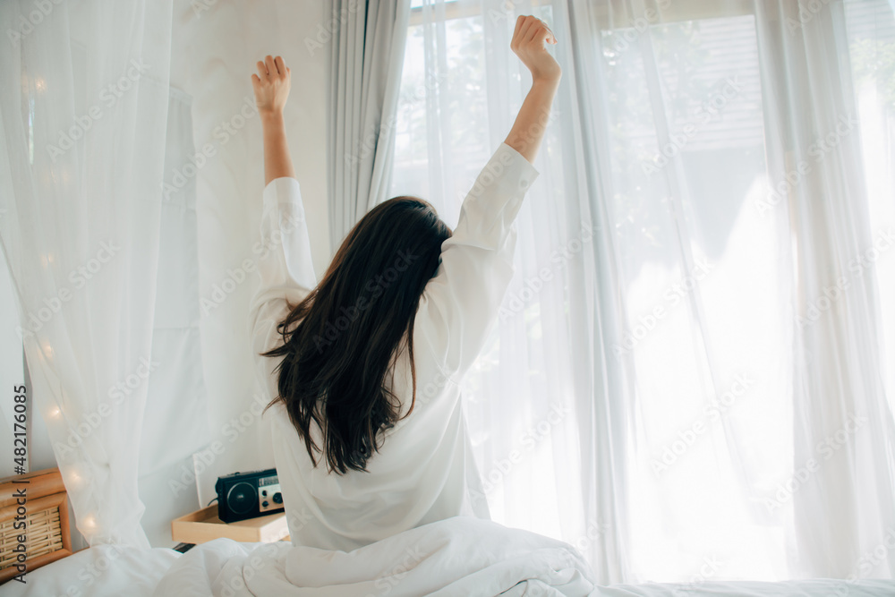 Young asian woman in white pajamas waking up in her bed sitting near ...