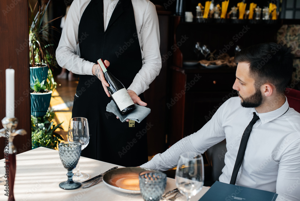 A young sommelier in a stylish uniform demonstrates and offers the ...