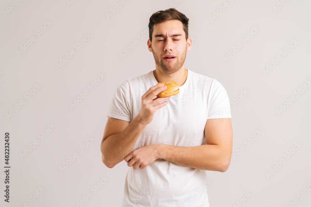 Portrait of hungry young man eating bad burger and suffering stomach ...