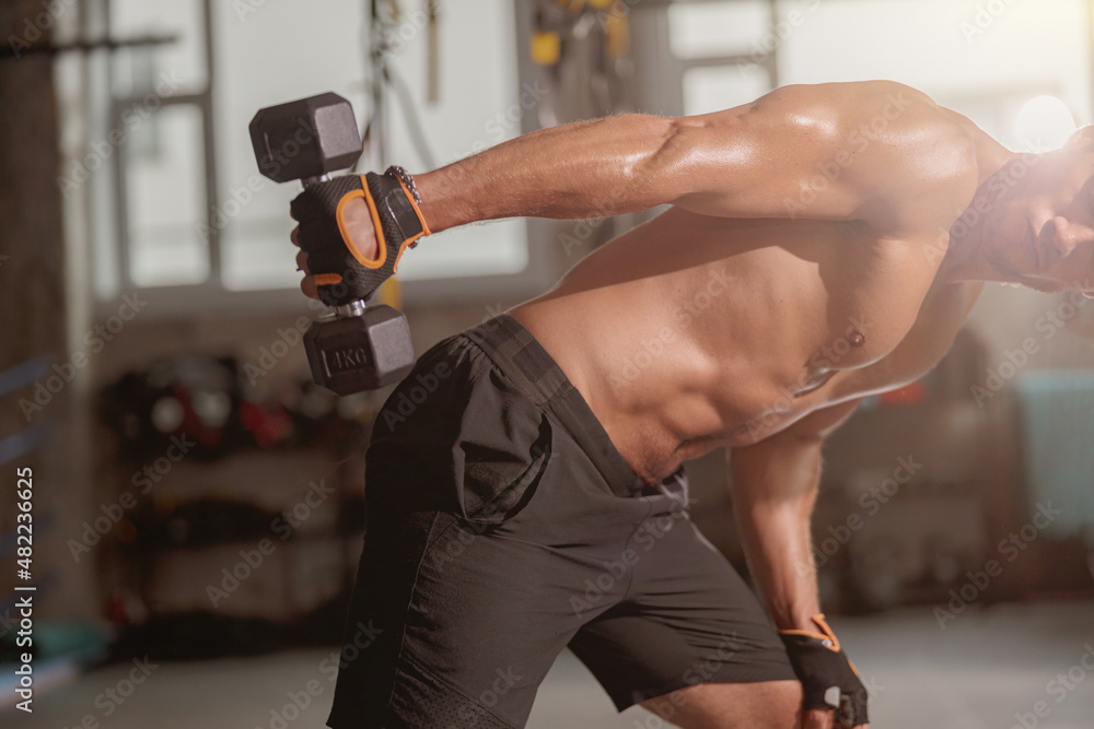 Athletic man in workout gloves standing, holding black dumbbell ...