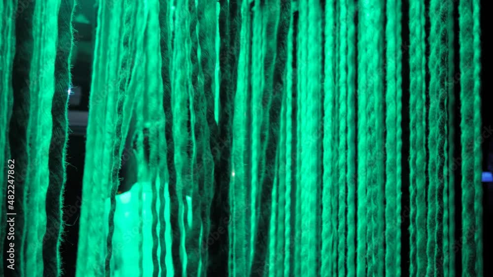 Woman walking through hanging ropes with colorful illumination in dark ...