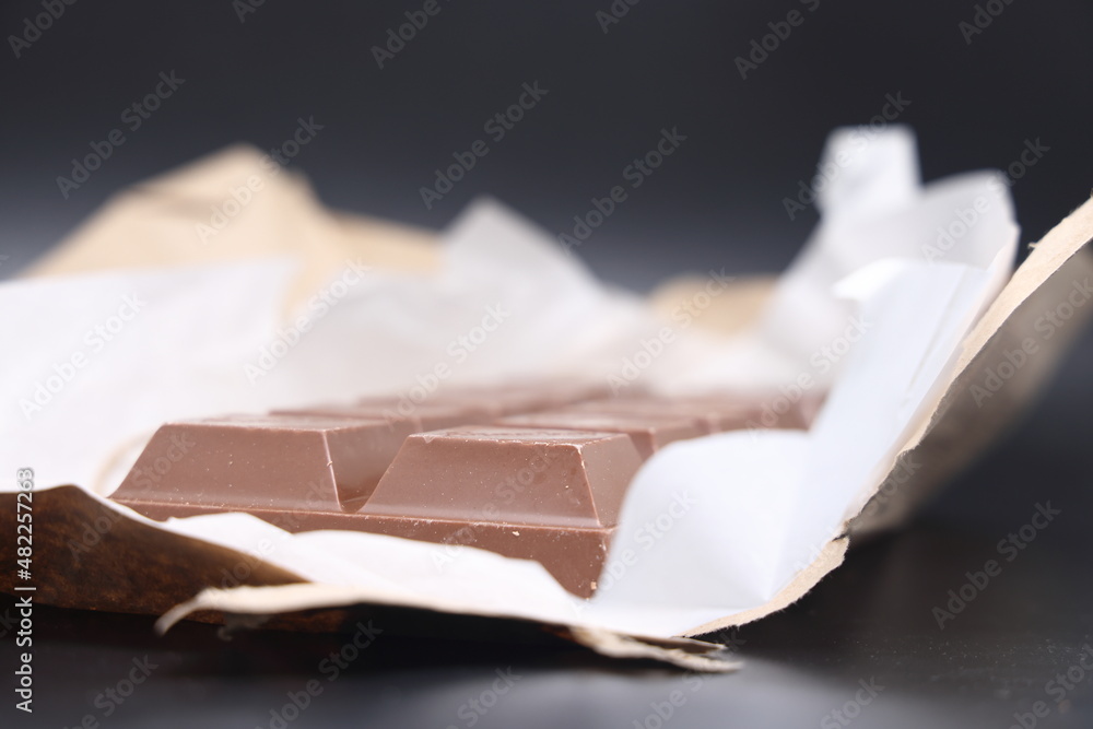 The photo shows a large bar of milk chocolate in an open wrapper. Stock ...