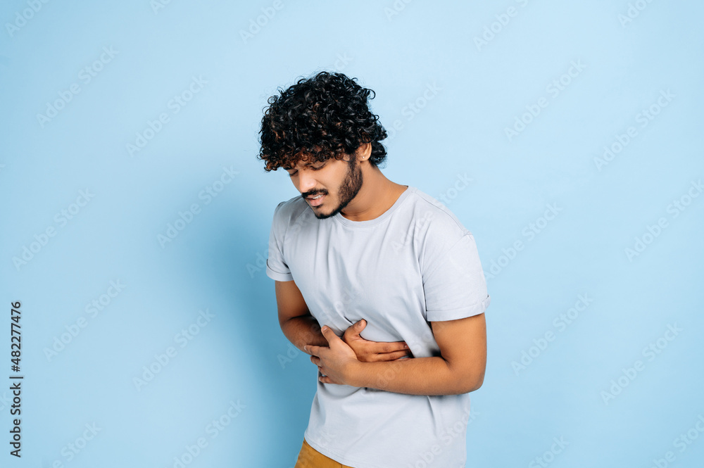 Stomach ache. Indian guy with in casual clothes hunching and holding ...