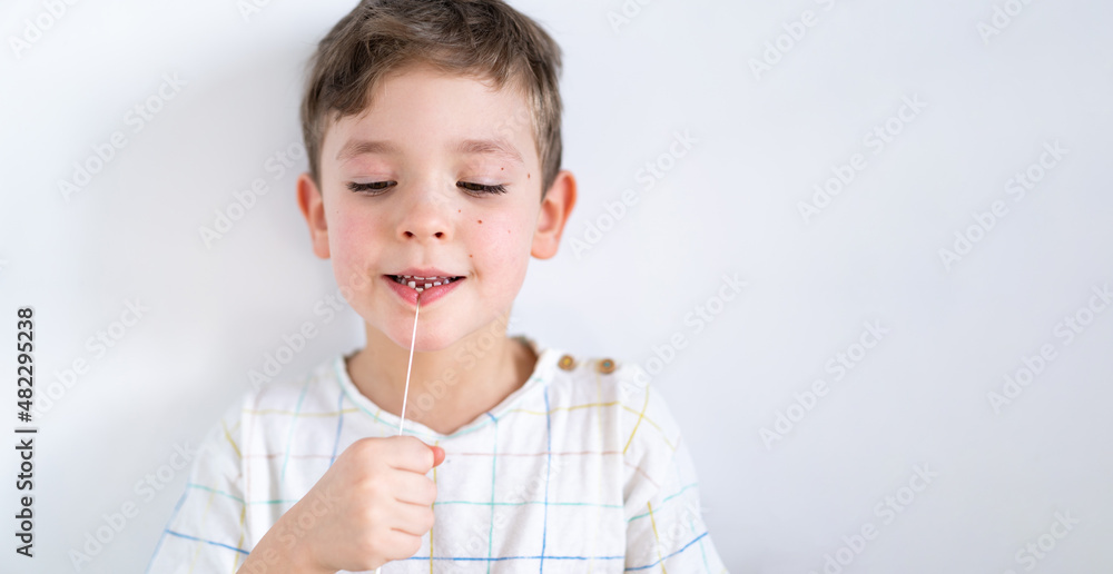 Cute boy pulling loose tooth using a dental floss. The boy's first milk tooth is loose ...