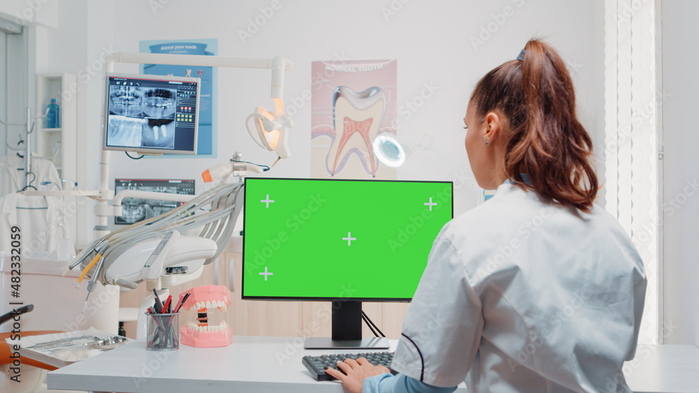 Woman using keyboard and computer with green screen in dental cabinet ...