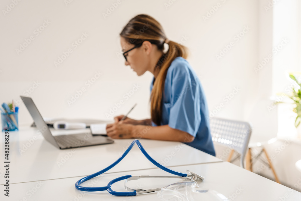 White woman doctor writing down notes while working with laptop Stock ...