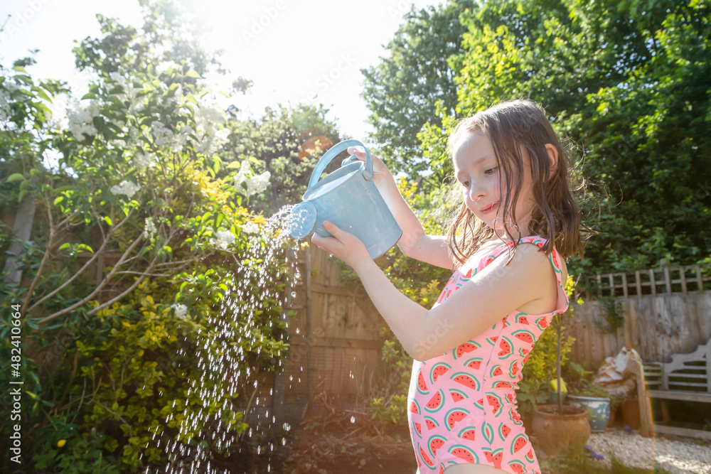 Girl (4-5) in swimsuit pouring water from watering can in garden Stock ...