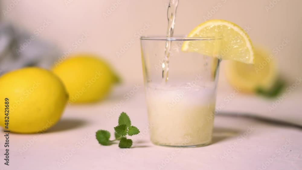 Pouring sparkling lemonade into the glass decorated with slice of lemon ...