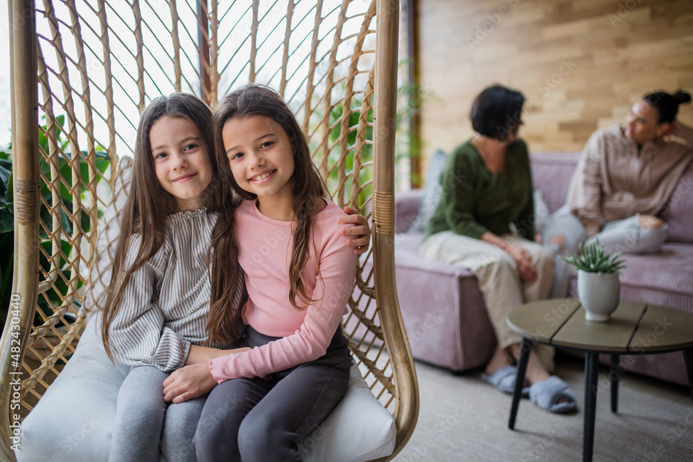 Happy little sisters sitting in wicker rattan hang chair indoors in ...