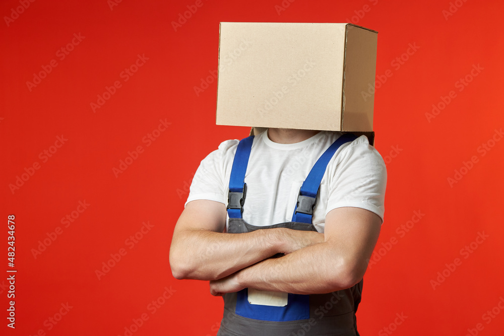 Funny loader in work clothes with a box on his head stands confidently ...