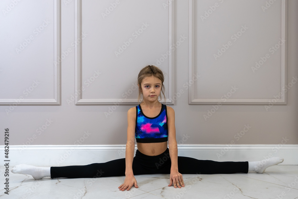 little girl in sports clothes doing split on the floor in a living room ...
