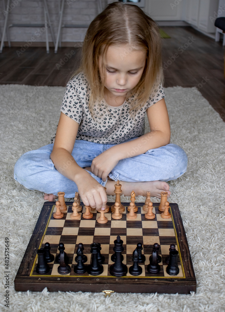 selective focus on child's hand and chess board, little girl sitting on ...