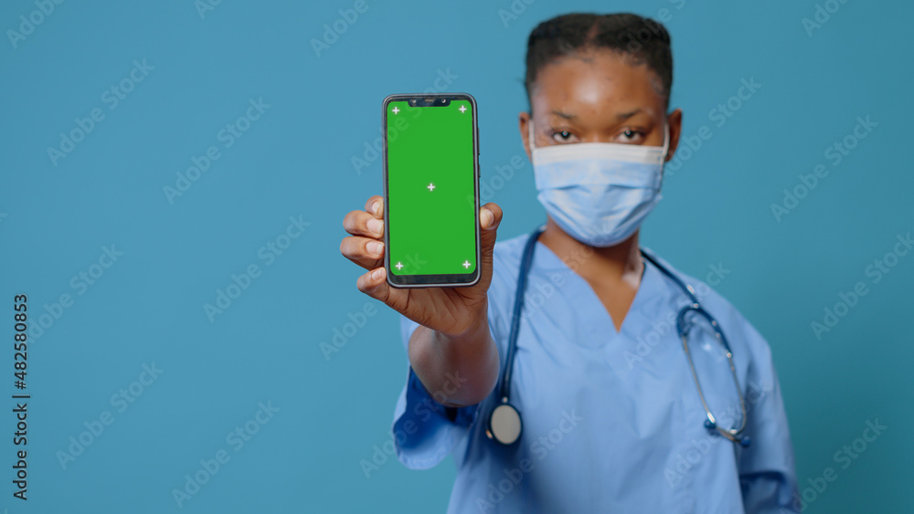 Woman nurse with face mask showing green screen on smartphone in studio ...