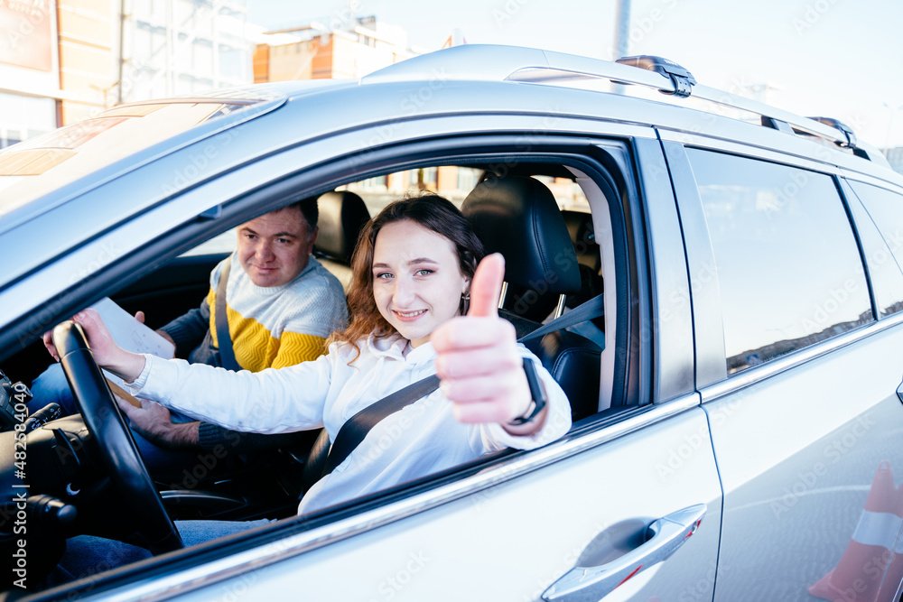 Smiling carefully young woman in drivers seat showing thumbs up gesture ...