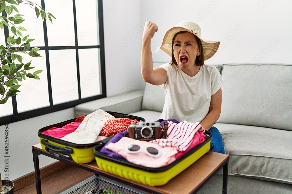 Beautiful middle age hispanic woman packing summer clothes in suitcase ...