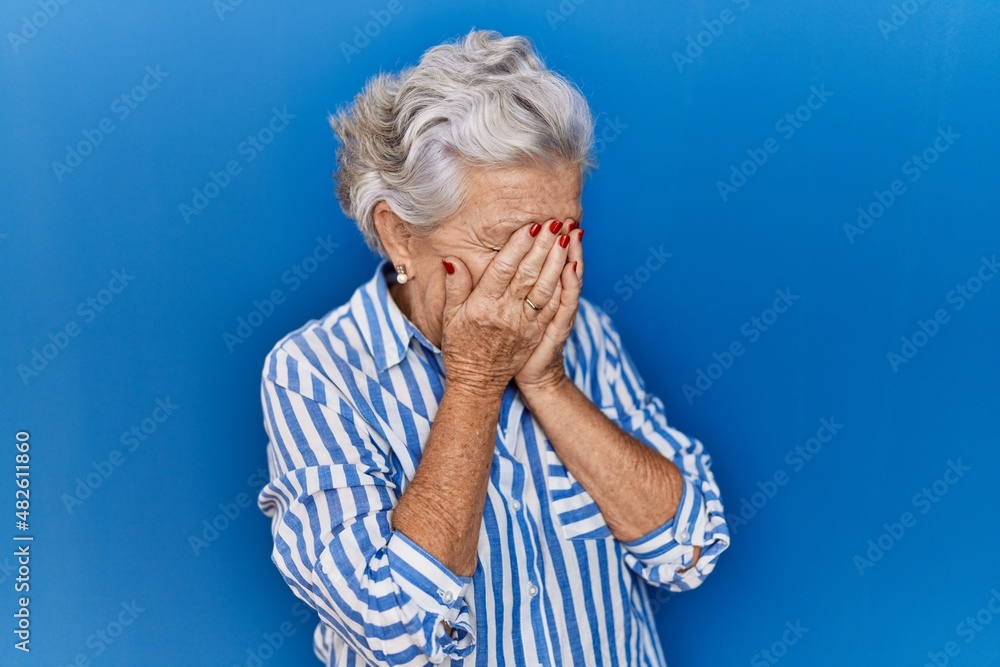 Senior woman with grey hair standing over blue background with sad ...