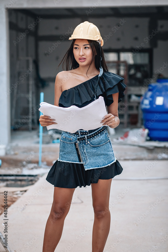 Beautiful young engineer in helmet and dress is designing a new ...