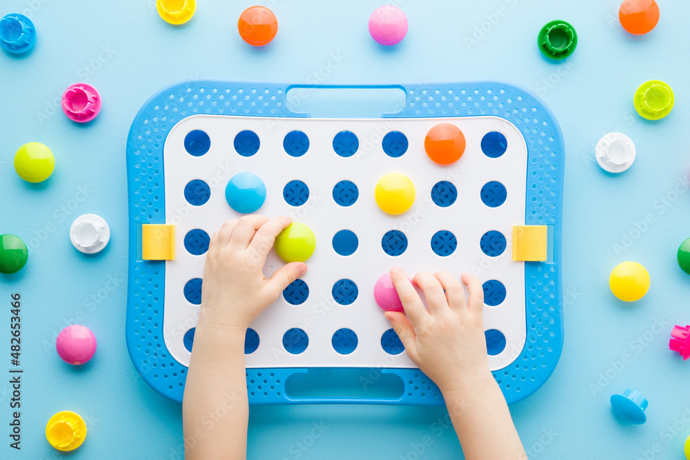 Baby boy hands playing and putting colorful plastic buttons in holes of ...