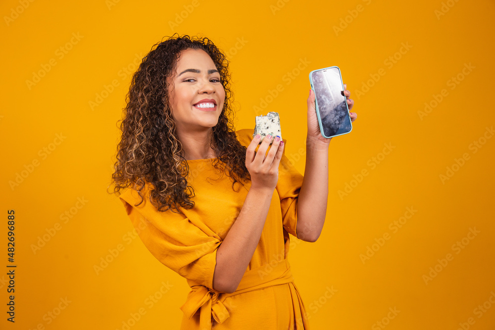 Foto de Woman holding a piece of cheese in one hand and cellphone in ...