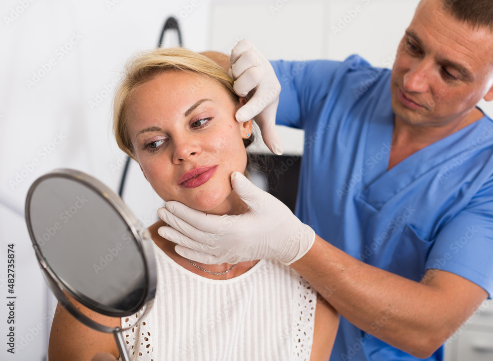 Specialist is analysing skin of female patient with using mirror before ...