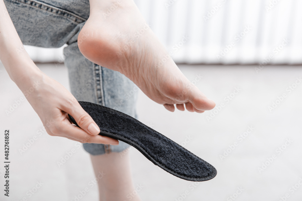Woman fitting orthopedic insole indoors, close up. Girl holding an ...