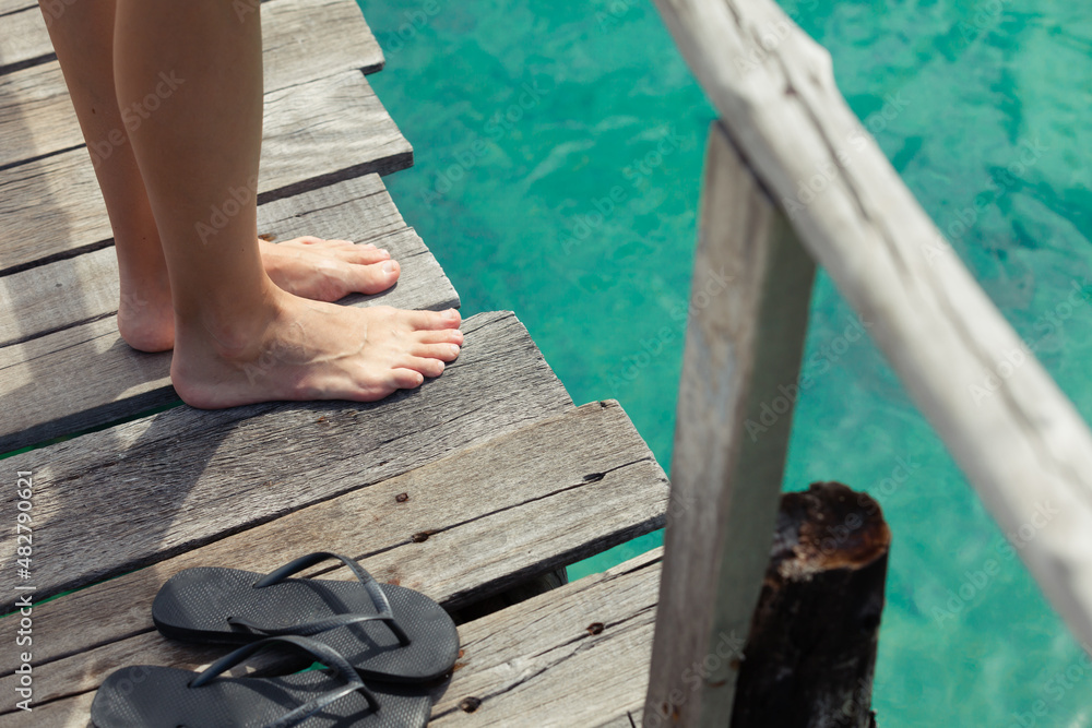 Female's feet standing on the pier looking down into the turquoise ...