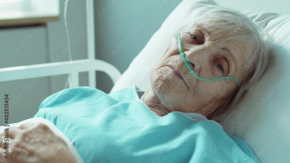 Portrait of elderly Caucasian woman with nasal cannula lying on bed in ...