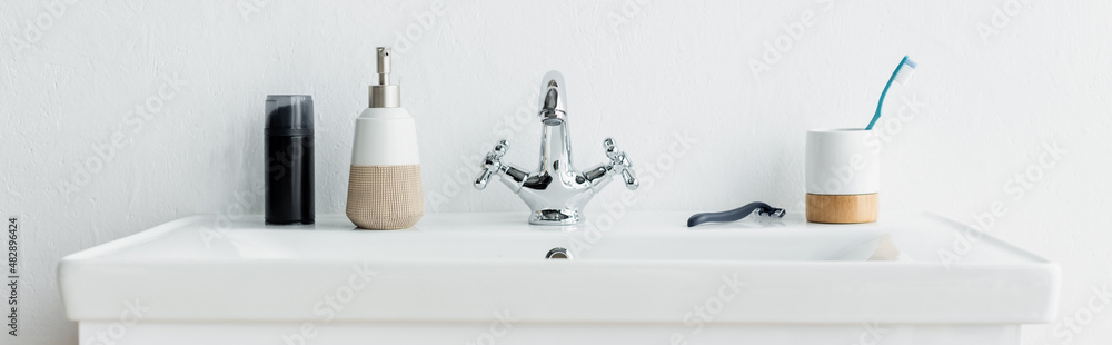 toothbrush, safety razor, liquid soap and shaving foam on white sink ...