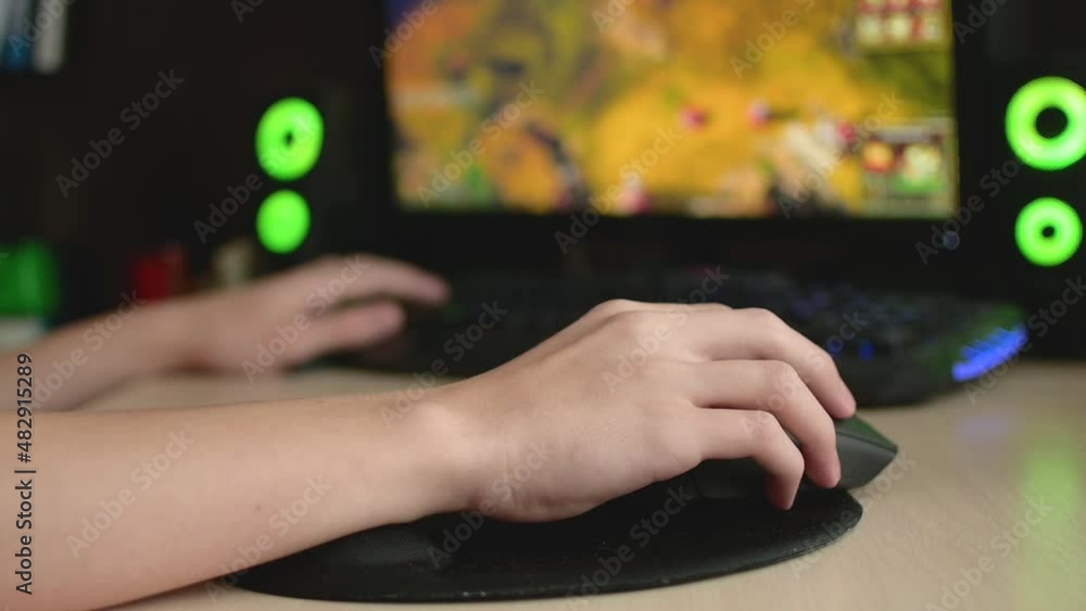 A teenage boy sitting at a table playing a computer game. The hand ...