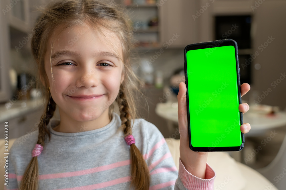 Happy smile little girl show smart phone with blank green screen mock ...