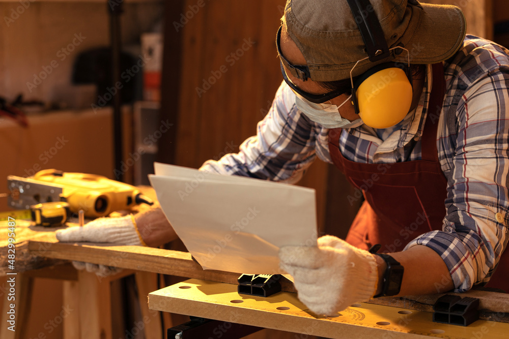Carpenter wearing safety ear muff with paper drawing while working in ...