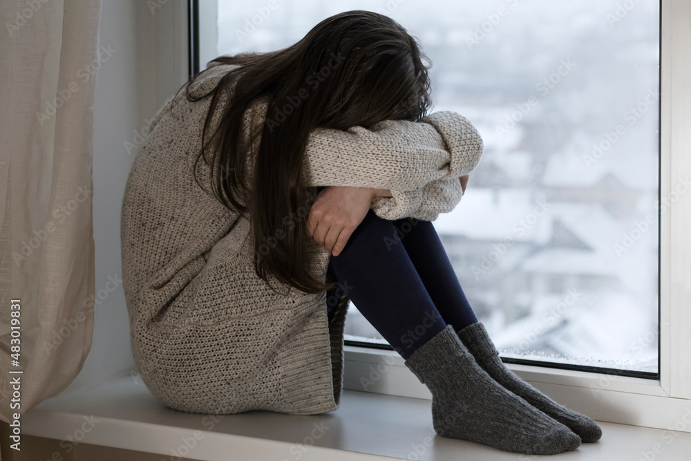 Stress, Depression. Lonely teen girl feeling depressed and stressed sitting by the window ...