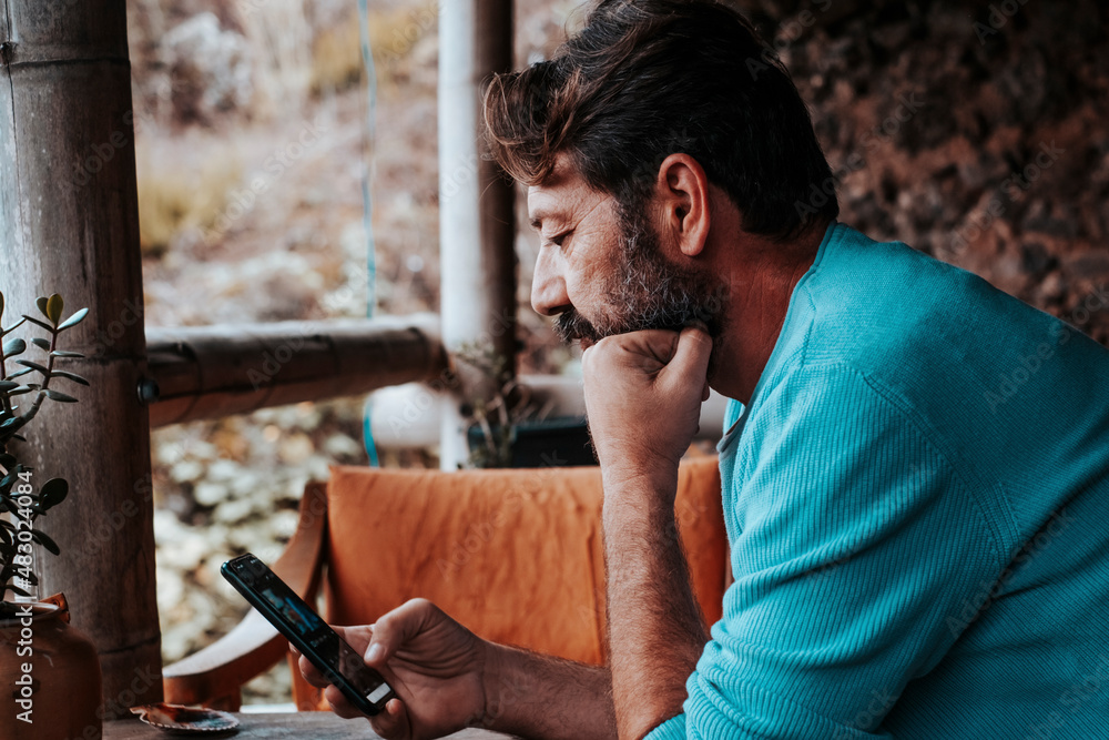 Mature man using and looking mobile phone worried at home. Modern adult ...